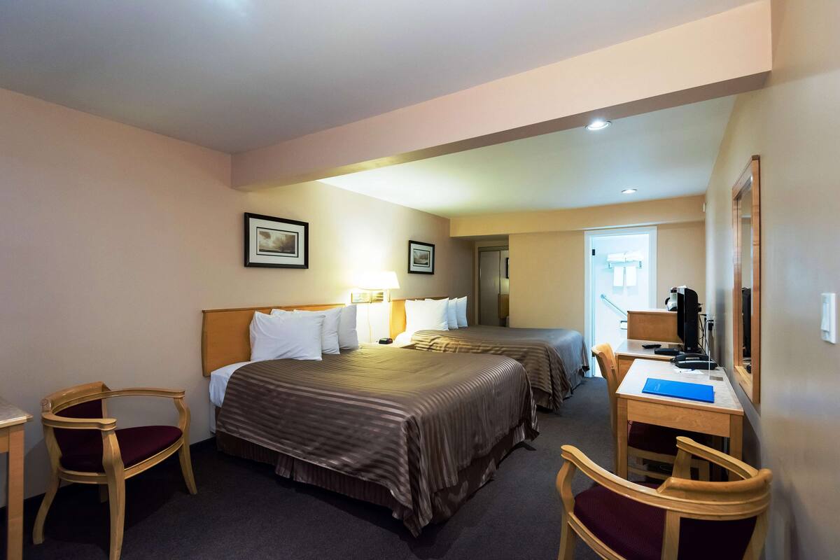 Quarto de hotel com duas camas, uma escrivaninha, uma cadeira e um espelho.
