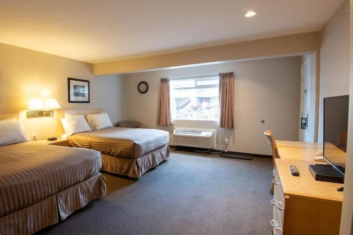 Quarto de hotel com duas camas, uma escrivaninha, uma cadeira, uma televisão e uma janela com cortinas.