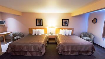 Quarto de hotel com duas camas, uma escrivaninha e duas cadeiras estampadas.