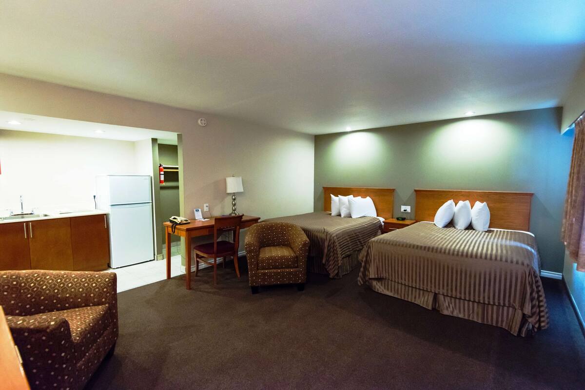 Quarto de hotel com duas camas, uma escrivaninha, uma cadeira e uma kitchenette.
