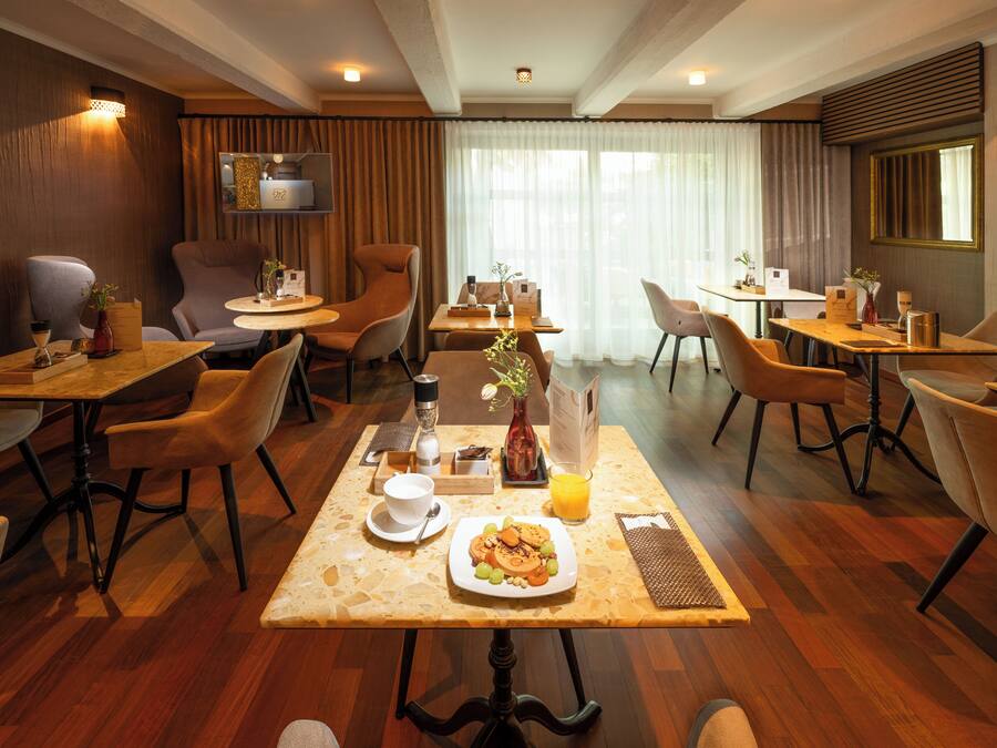 Uma sala de jantar de hotel com várias mesas e cadeiras, uma máquina de café e uma variedade de opções para o pequeno-almoço.