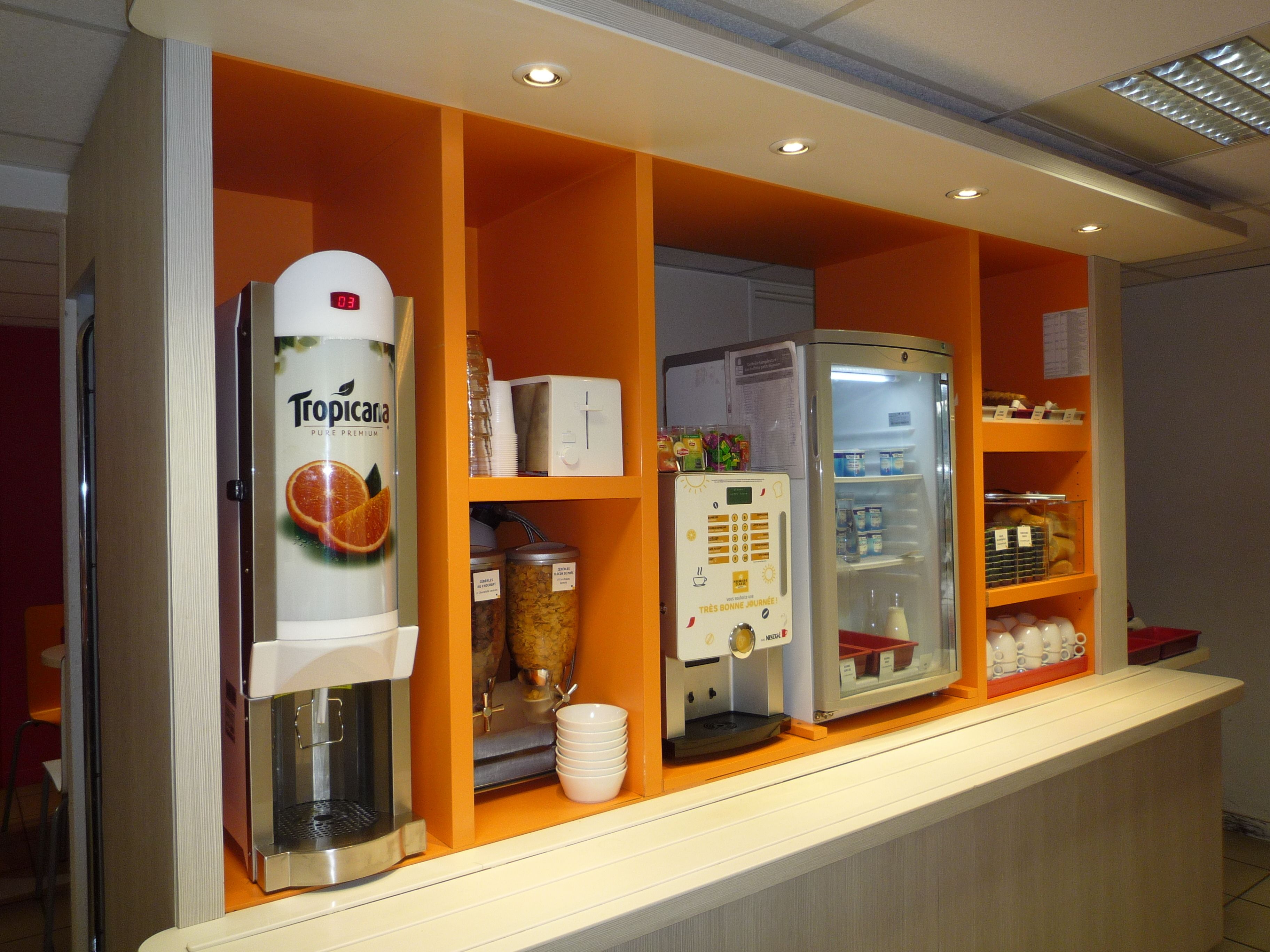 Uma estação de bebidas com serviço próprio, incluindo máquina de café, refrigerador e diversos alimentos.