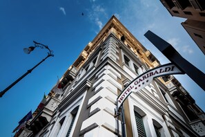 Placa de hotel com a inscrição 'HOTEL CARIBALDI', céu azul claro e um poste de luz.