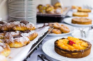 Diversos pastéis e sobremesas sobre uma mesa, incluindo croissants, donuts e uma tarte de fruta.