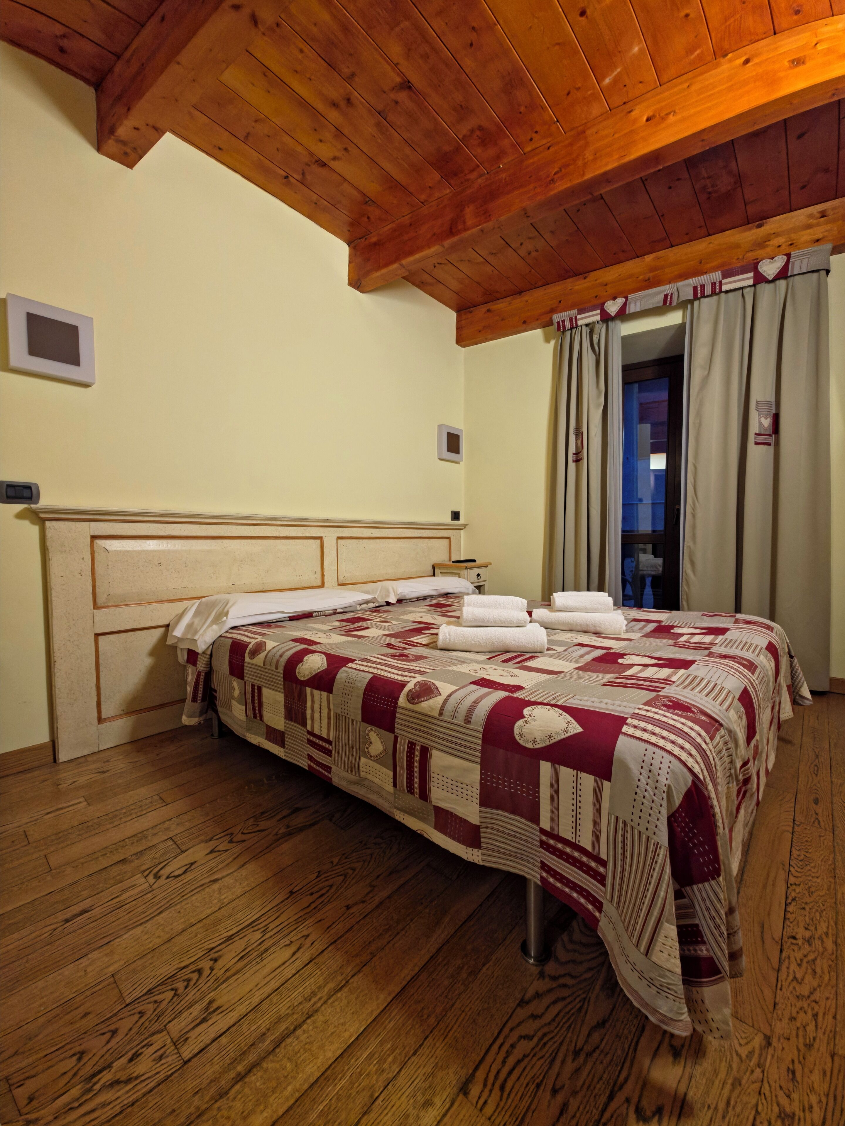 Um quarto com teto de madeira, uma cama com colcha estampada e uma mesinha de cabeceira.