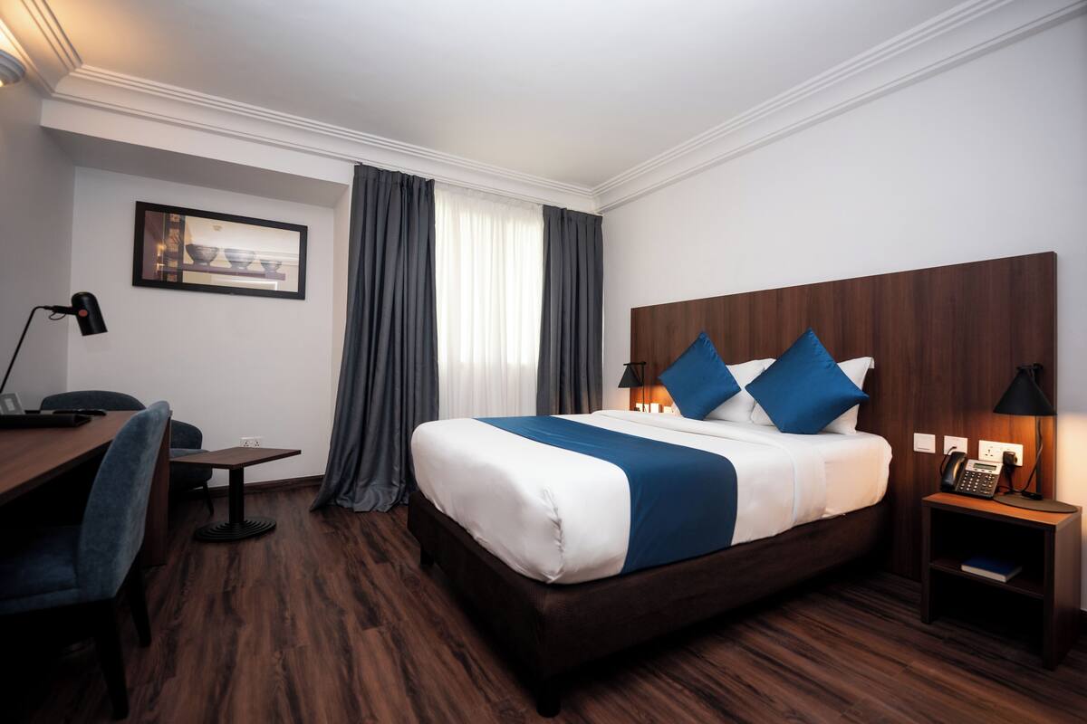 Quarto de hotel com cama de madeira, uma escrivaninha e uma cadeira.