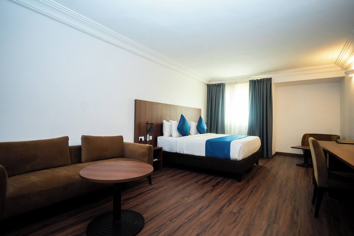 Quarto de hotel com cama, sofá, mesa redonda e escrivaninha.