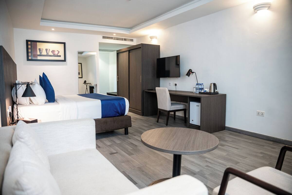 Quarto de hotel moderno com uma cama, escrivaninha, cadeira, mesa redonda e uma televisão.