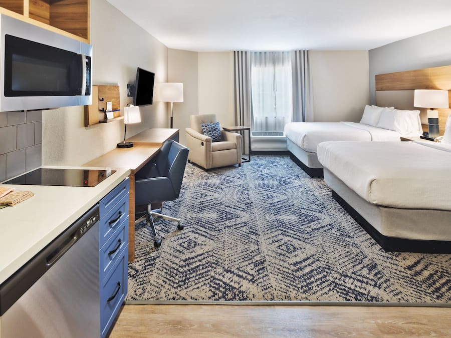 Quarto de hotel com cozinha compacta, duas camas, uma escrivaninha e televisão.