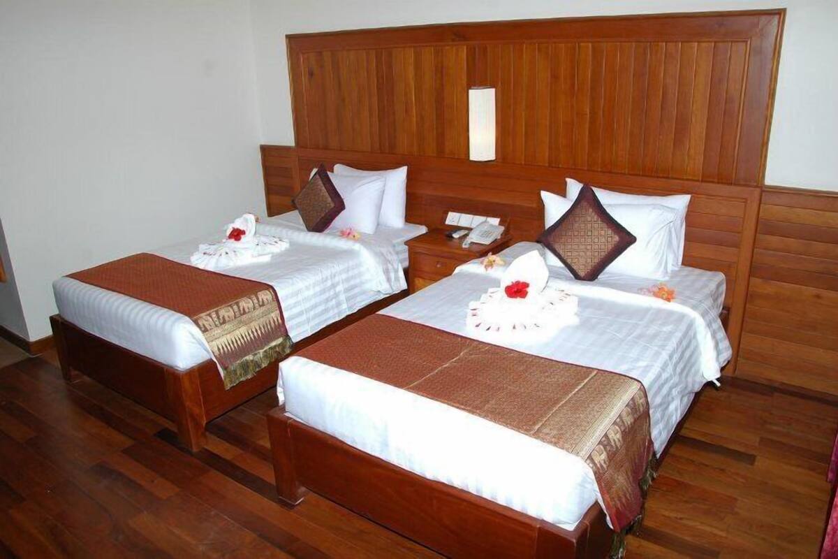 Quarto de hotel com duas camas de madeira, cada uma com colcha branca e almofadas decorativas.