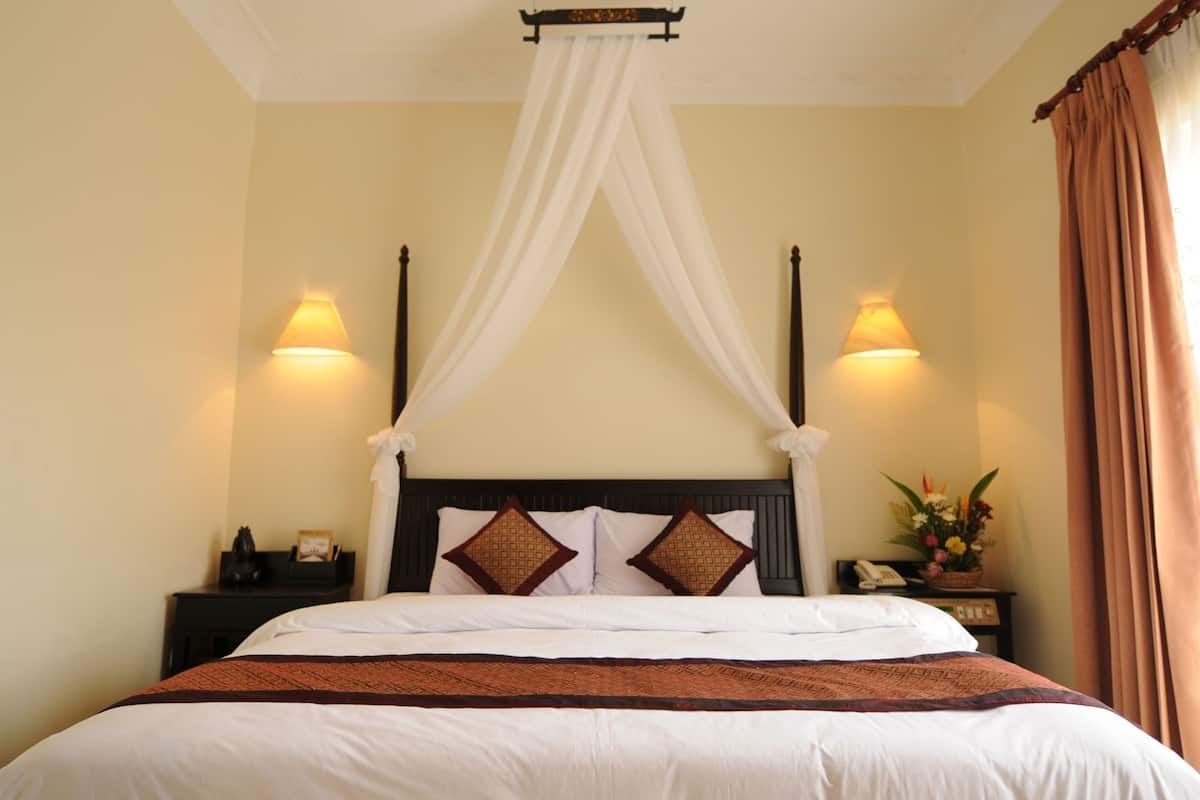 Cama com dossel, abajures, mesa de cabeceira com telefone e um arranjo de flores.