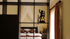 Quarto de hotel com uma cama, uma mesa de cabeceira com telefone e um vaso, e um objeto decorativo na parede.