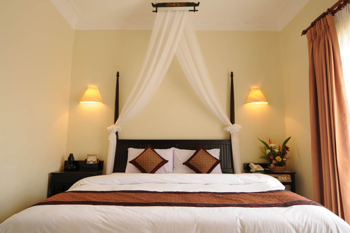 Uma cama com dossel, duas luminárias de cabeceira, um criado-mudo com telefone e um arranjo floral.