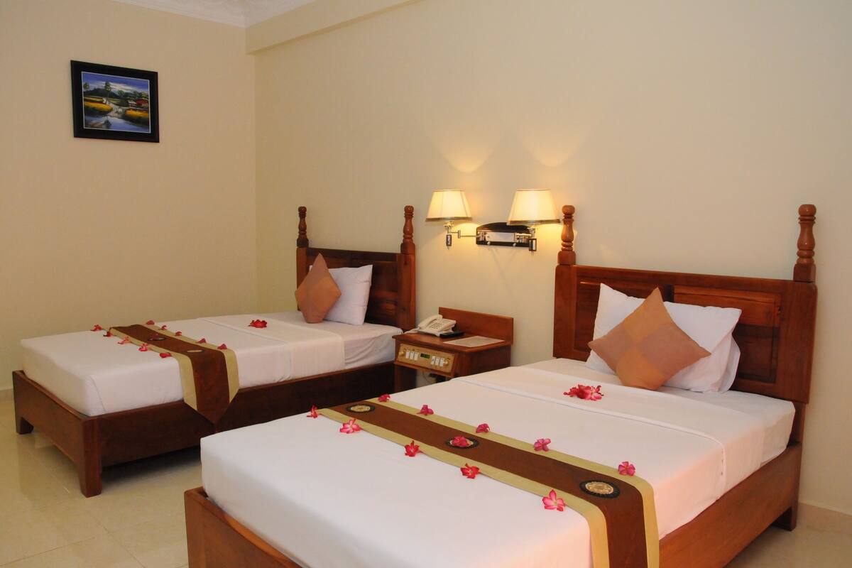Duas camas de casal com estrutura de madeira, roupa de cama branca e guirlandas decorativas de flores.