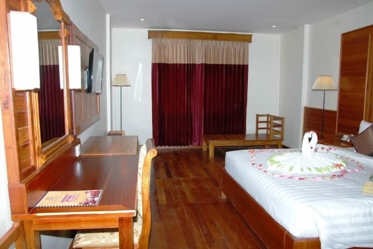 Quarto de hotel com cama de madeira, escrivaninha, cadeira, televisão e janela com cortinas.