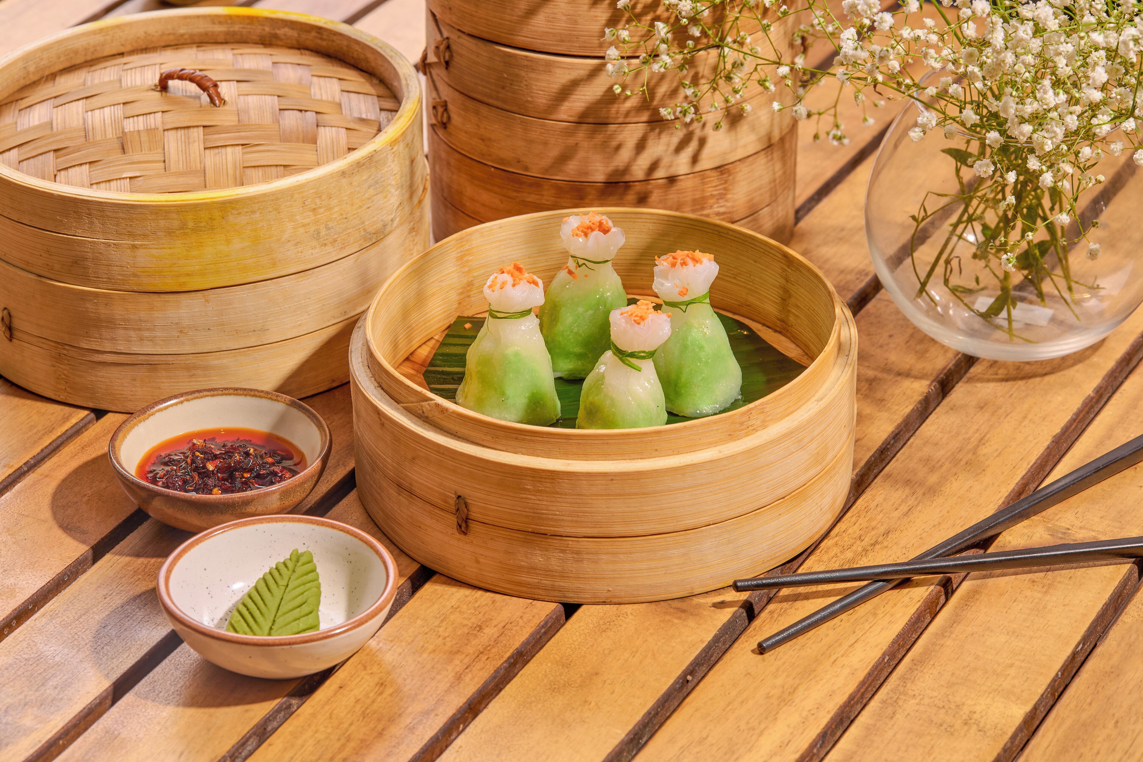 Um cestinho de bambu com bolinhos verdes e uma pequena tigela de molho.