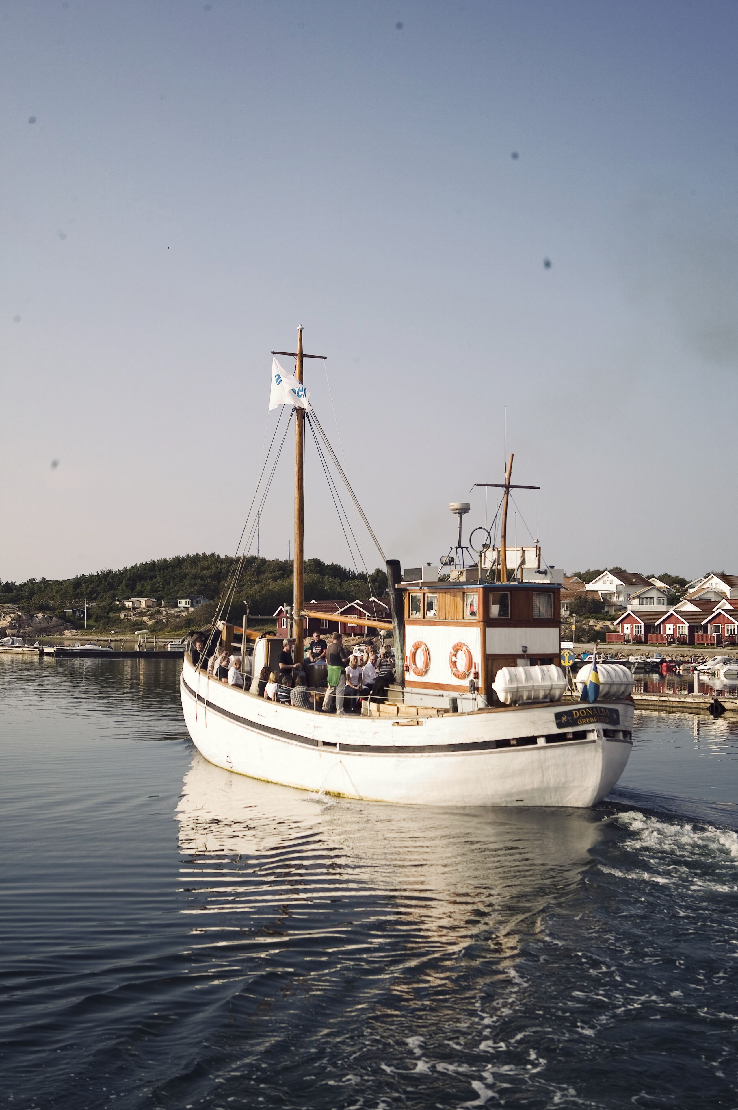 Um barco com passageiros atracado perto de uma orla, com casas ao fundo.