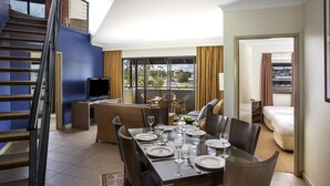 Uma área de jantar com mesa posta para quatro pessoas, televisão e varanda com mobiliário de exterior.