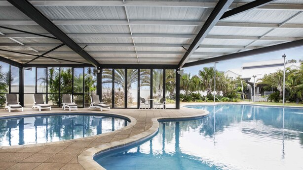 Piscina com espreguiçadeiras e área coberta com grandes janelas.