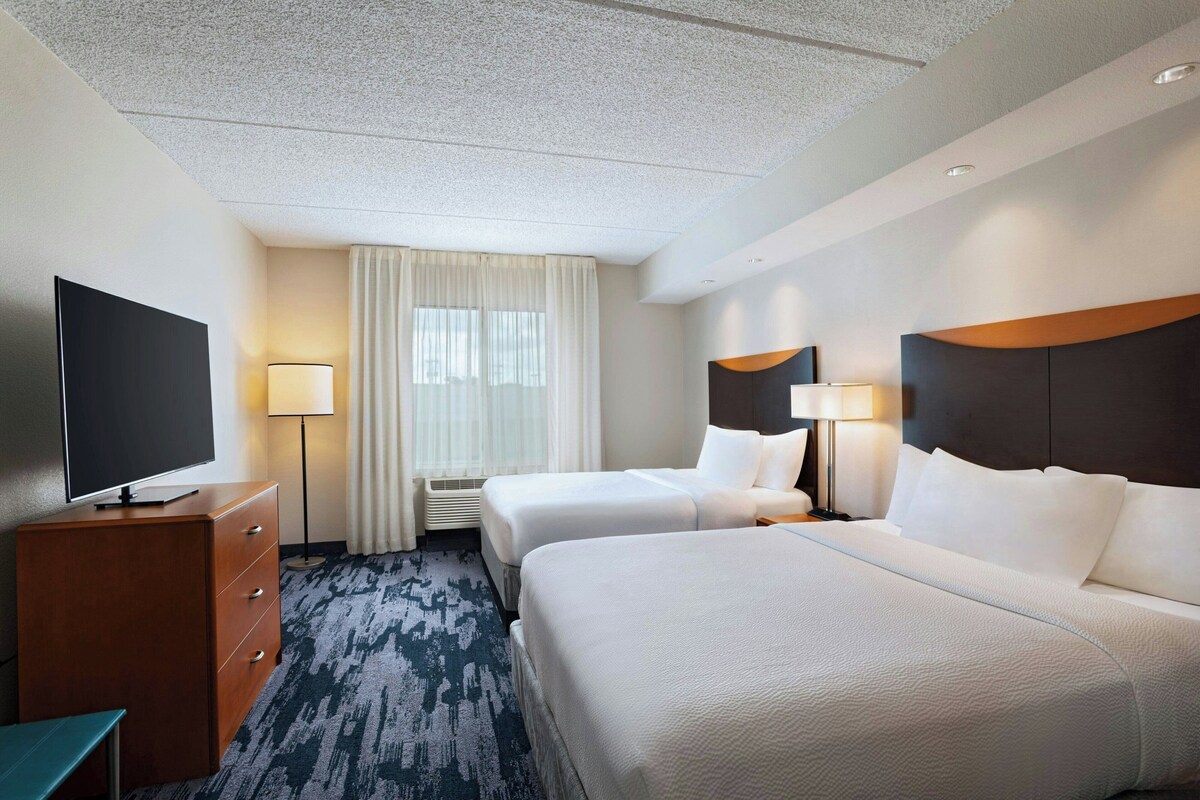 Quarto de hotel com duas camas, televisão, escrivaninha e abajur.