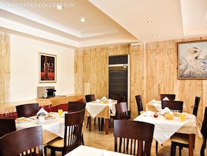 Uma área de jantar com mesas para quatro pessoas, painéis de madeira nas paredes e um quadro sobre as mesas.