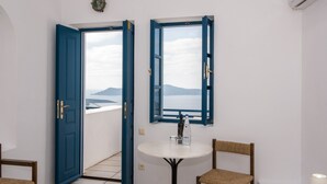 Quarto com porta azul e janela, mesa redonda com cadeiras, e vista para o mar.