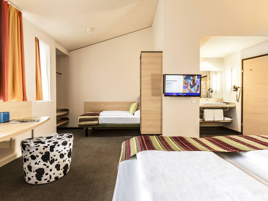 Quarto de hotel com cama, escrivaninha, televisão e banheiro.