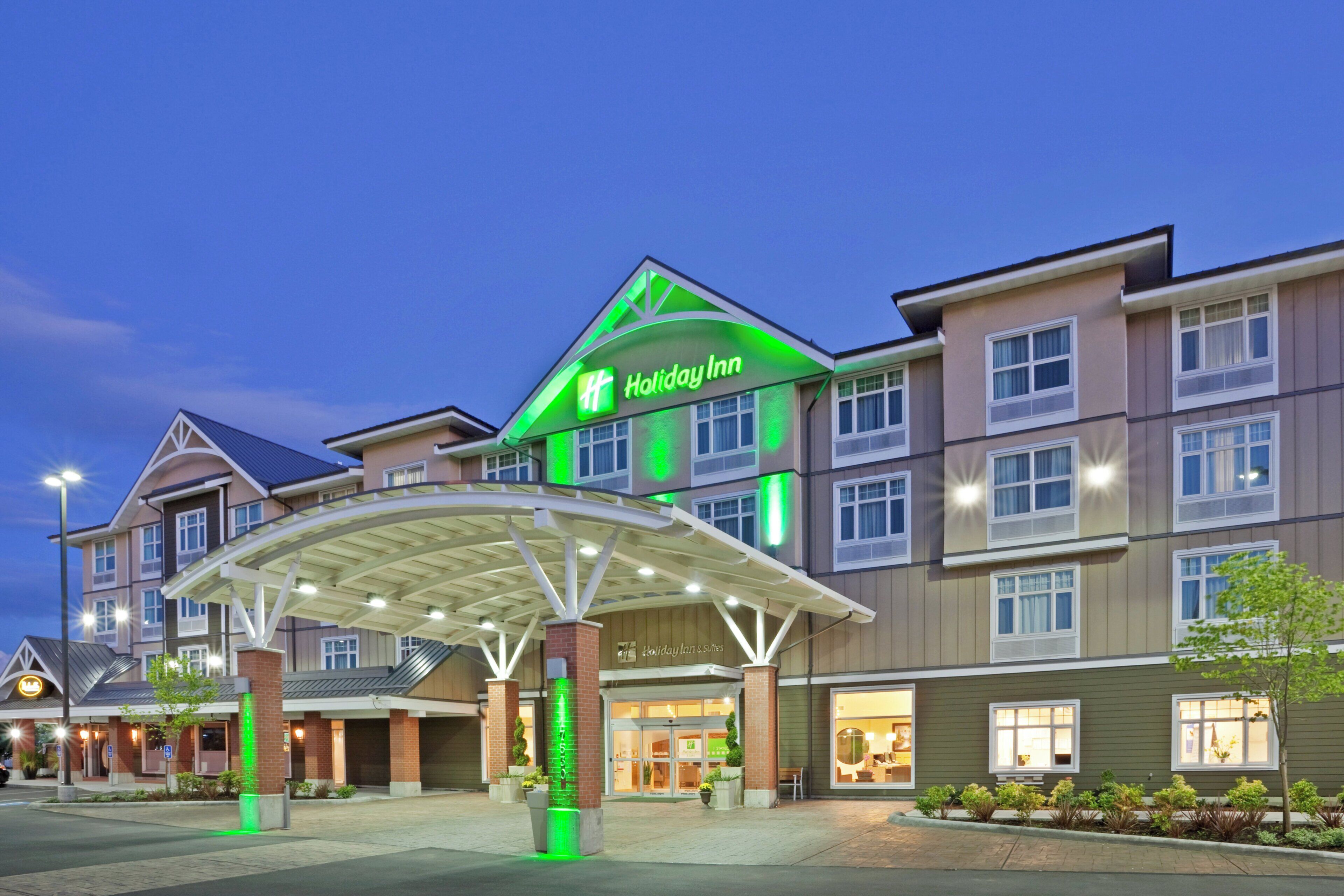 Um hotel Holiday Inn com entrada coberta, vários andares e fachada bem iluminada.