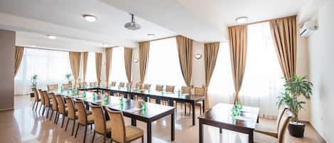 Uma sala de conferências com uma mesa comprida, várias cadeiras e plantas em vasos.