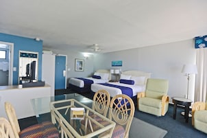 Quarto de hotel com uma cama, duas cadeiras, uma mesa, um abajur e um ventilador de teto.