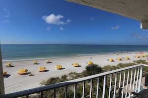 Vista da praia a partir de uma varanda, com guarda-sóis e espreguiçadeiras amarelas.