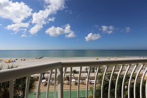 Vista da praia a partir de uma varanda com grade, praia de areia e mar calmo.