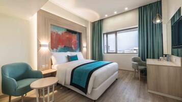 Quarto de hotel moderno com cama, escrivaninha, poltrona e vista para a cidade.