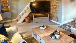 Uma sala de estar aconchegante com lareira, um sofá, uma mesa de centro e uma escada que leva a um andar superior.