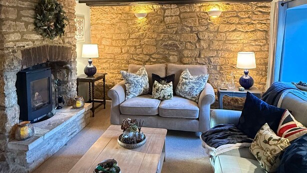Uma sala de estar aconchegante com lareira de pedra, sofás, mesa de centro e uma luminária.