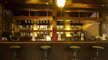 Um bar com várias prateleiras de garrafas, um vaso vermelho e luminárias pendentes.