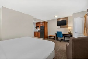 Quarto de hotel com cama, escrivaninha, cadeira, televisão e cozinha compacta.