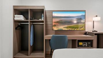 Quarto de hotel com um guarda-roupa de madeira, uma secretária com um computador, uma cama e um quadro grande com uma paisagem na parede.