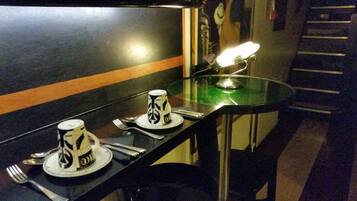 Uma mesa com uma luminária verde, duas xícaras e talheres.