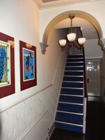 Uma escadaria com degraus azuis, um candelabro e dois cartazes emoldurados na parede.