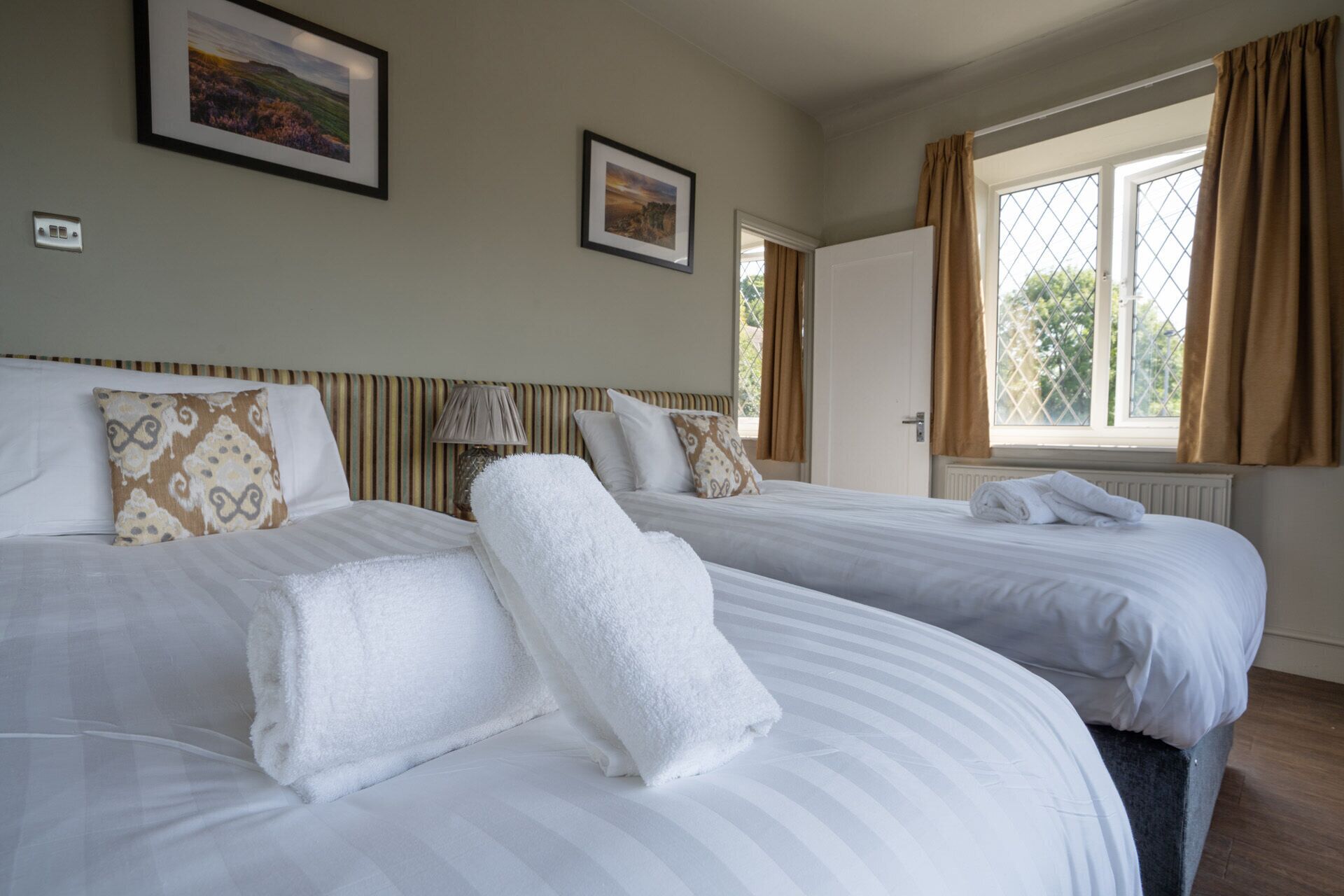 Quarto de hotel com duas camas, uma janela com cortinas e duas molduras com quadros na parede.