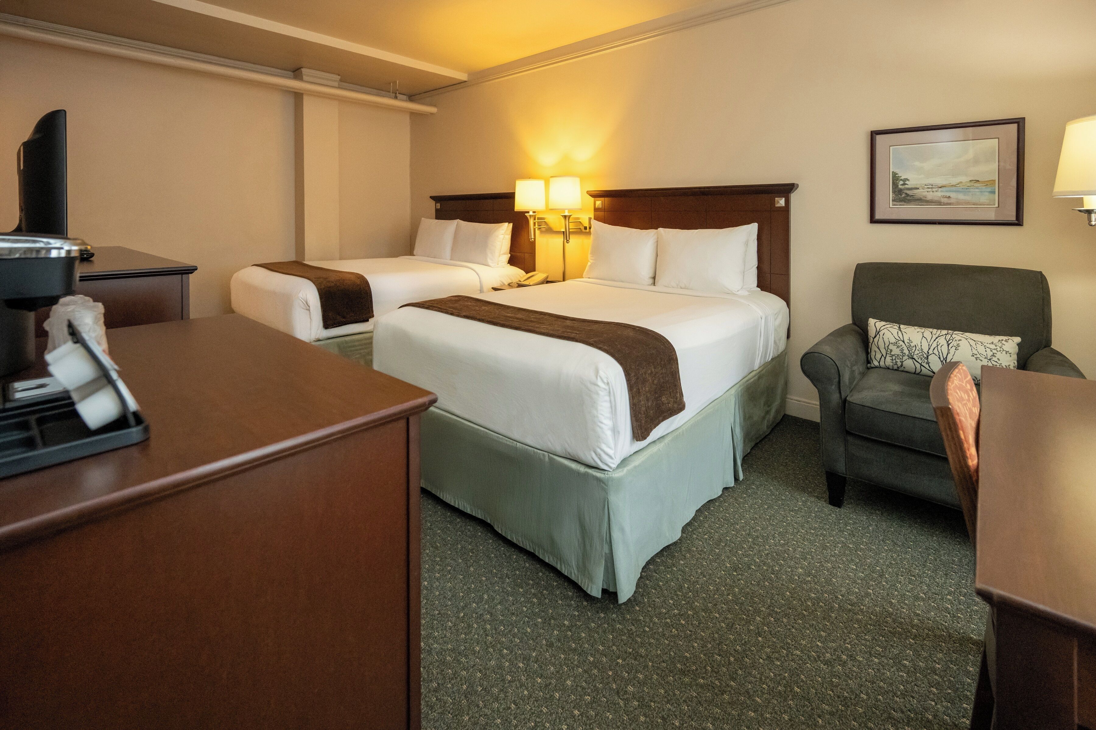 Quarto de hotel com duas camas, uma escrivaninha, uma cadeira e uma televisão.