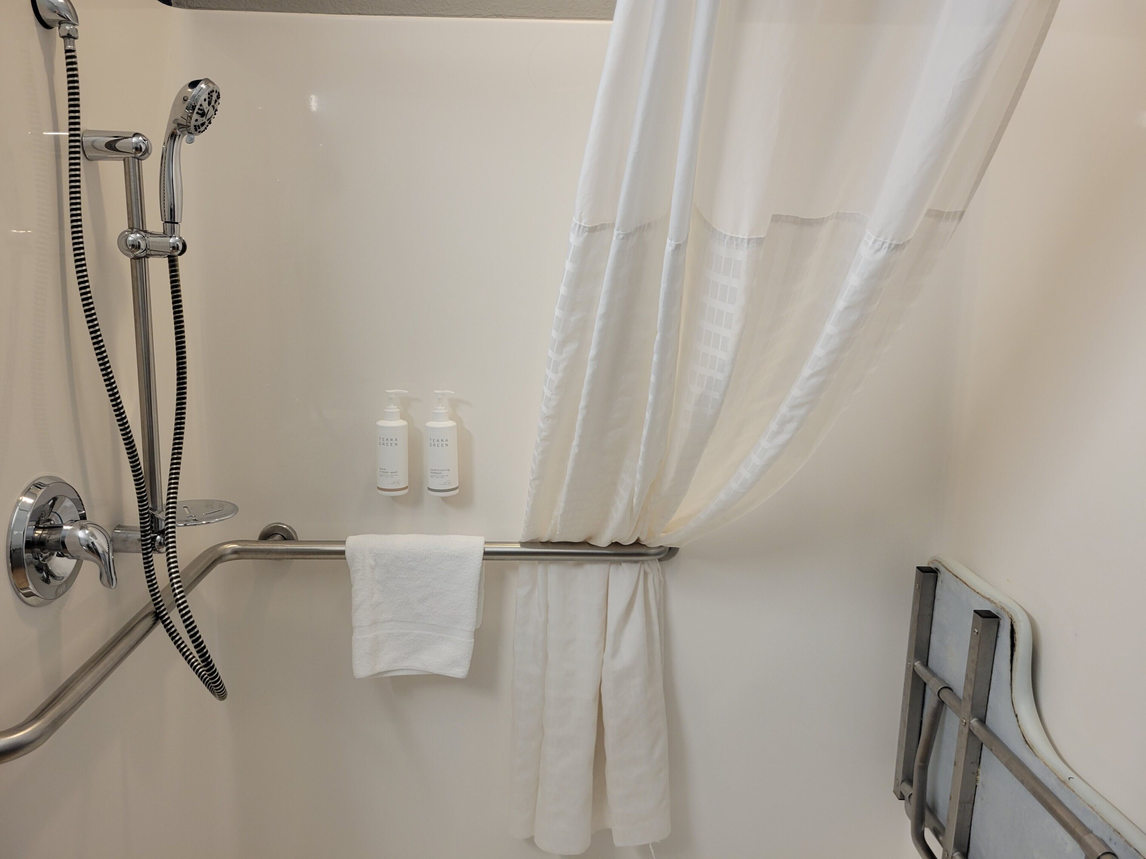 Área de duche com porta de vidro, um porta-toalhas com toalha branca e duas embalagens de gel de banho Terra Green.