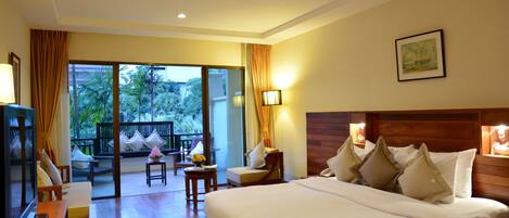 Quarto de hotel com uma cama grande, uma escrivaninha, uma cadeira e uma varanda com vista para o verde.