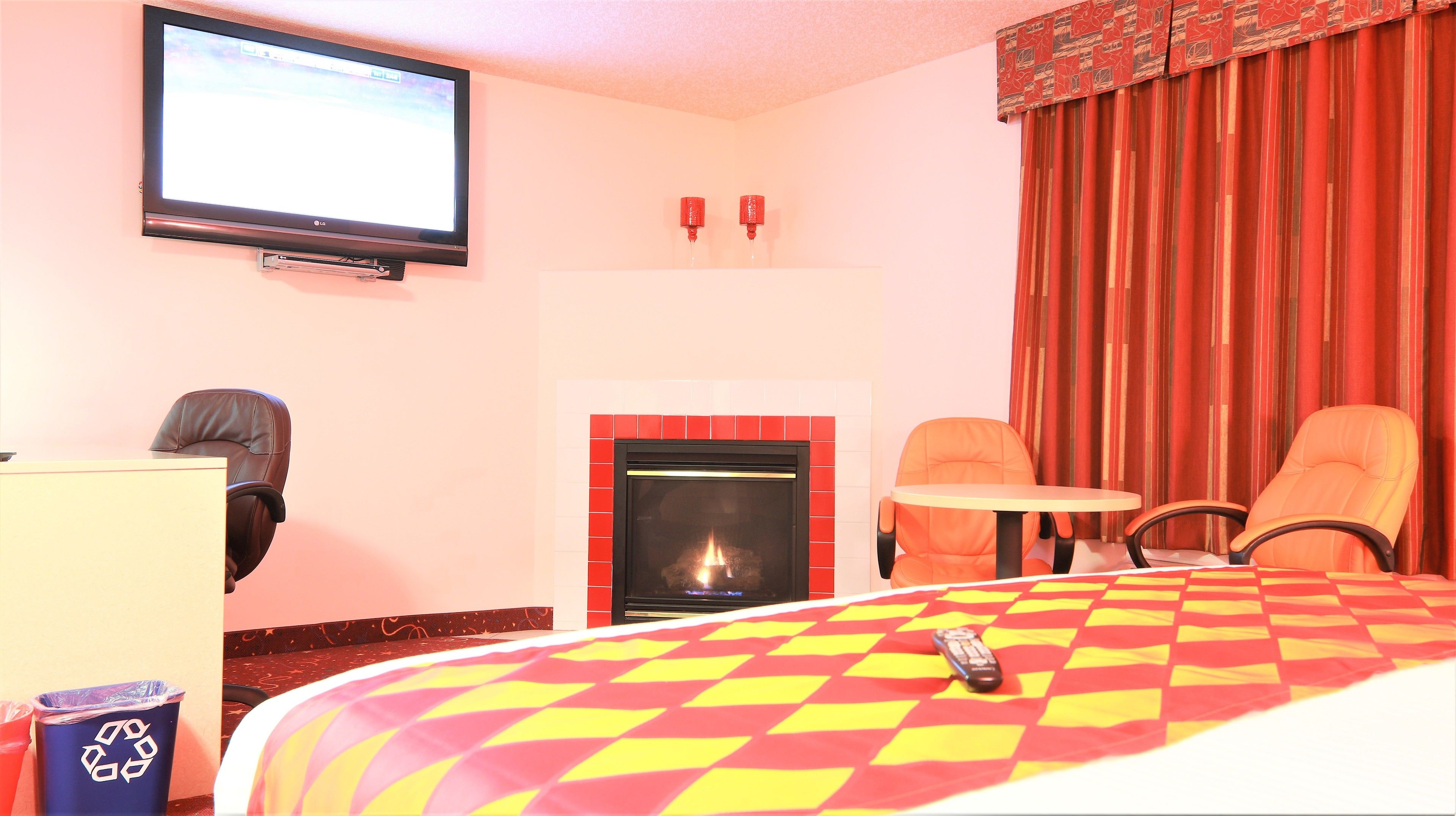 Quarto de hotel com cama, televisão, lareira, duas cadeiras e uma mesa pequena.