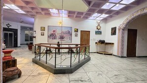 Um hall amplo com piso de mármore, guarda-corpo de vidro central e uma grande pintura na parede.