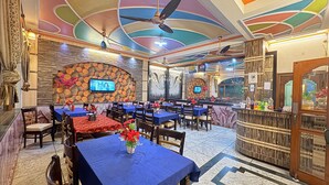 Restaurante com várias mesas, ventiladores no teto e uma tela de televisão.