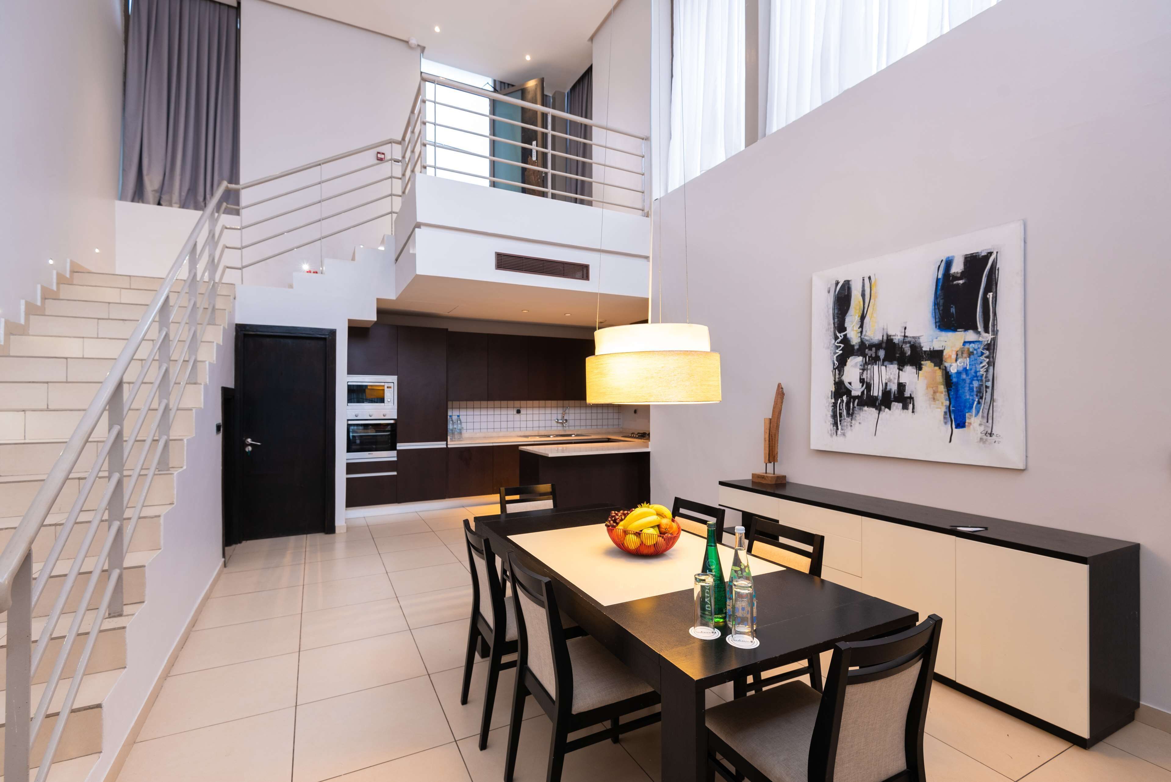 Uma cozinha moderna com área de jantar, apresentando uma escada, uma mesa de jantar com cadeiras, uma fruteira e um quadro na parede.
