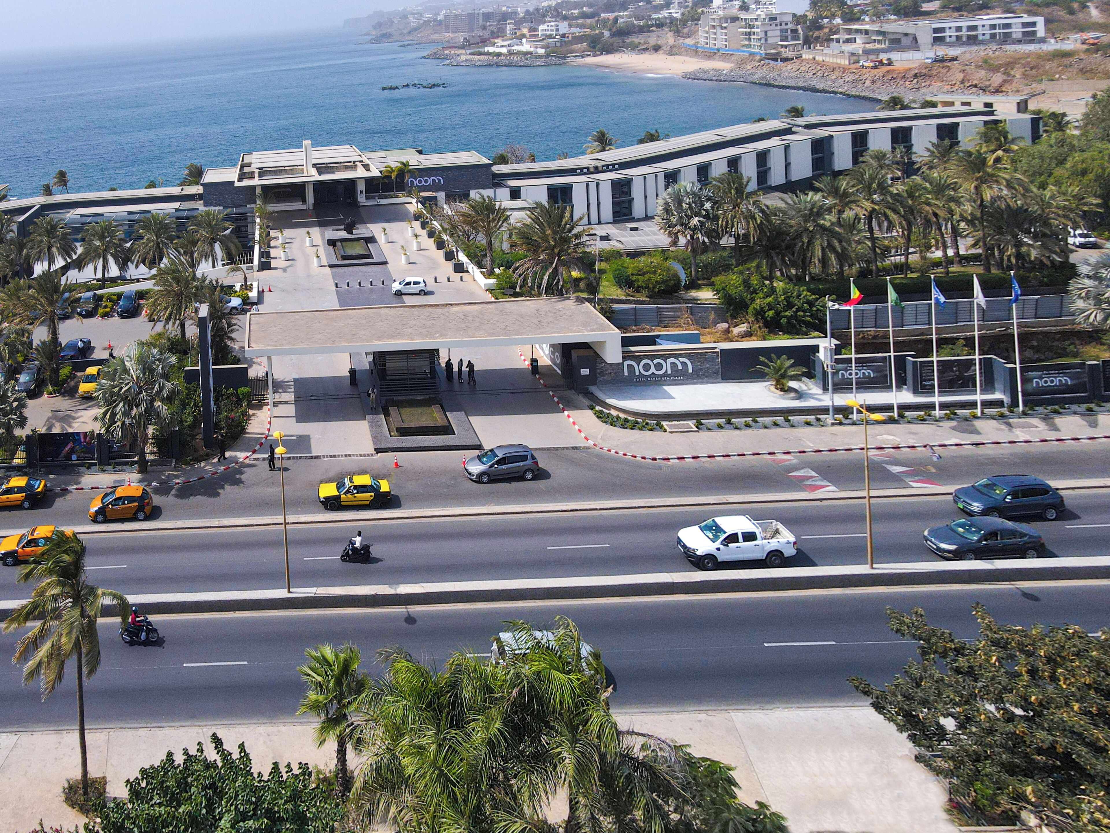 Um hotel moderno com vista para o mar, área de estacionamento e rua com veículos.