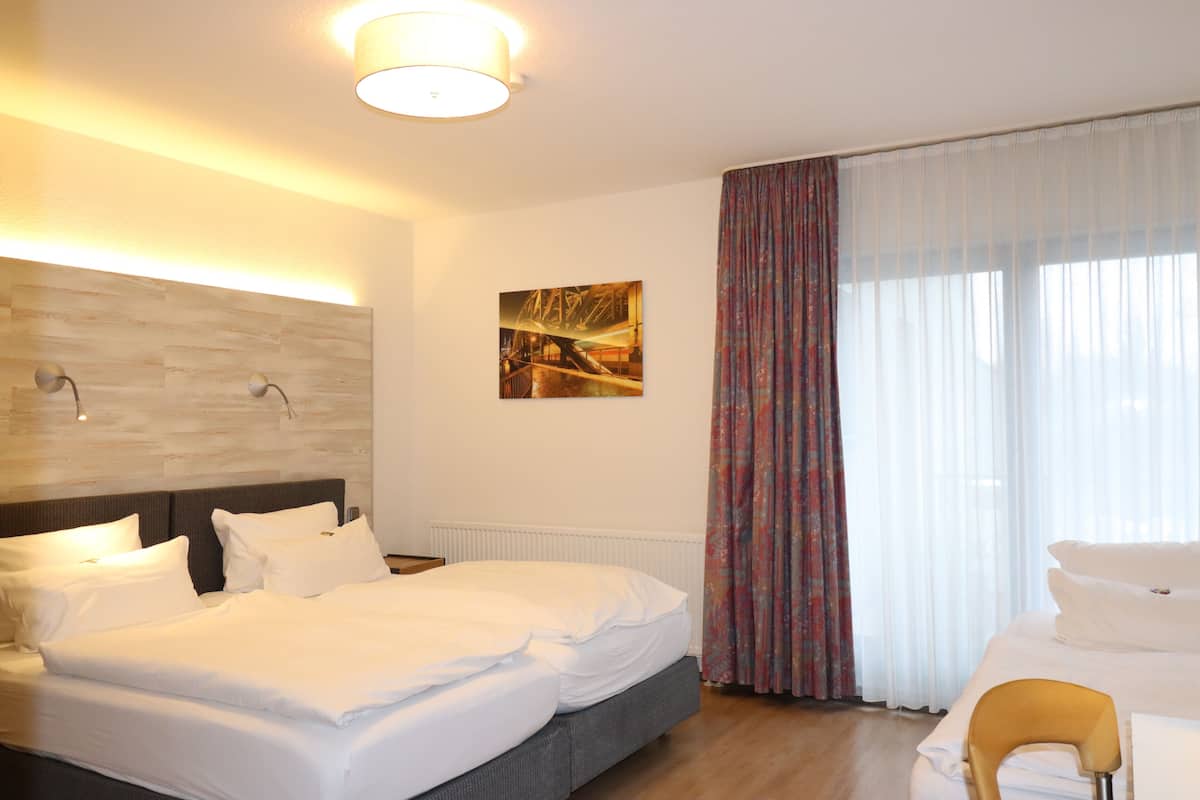 Quarto de hotel com uma cama grande, cabeceira, quadro na parede e janela com cortinas finas.